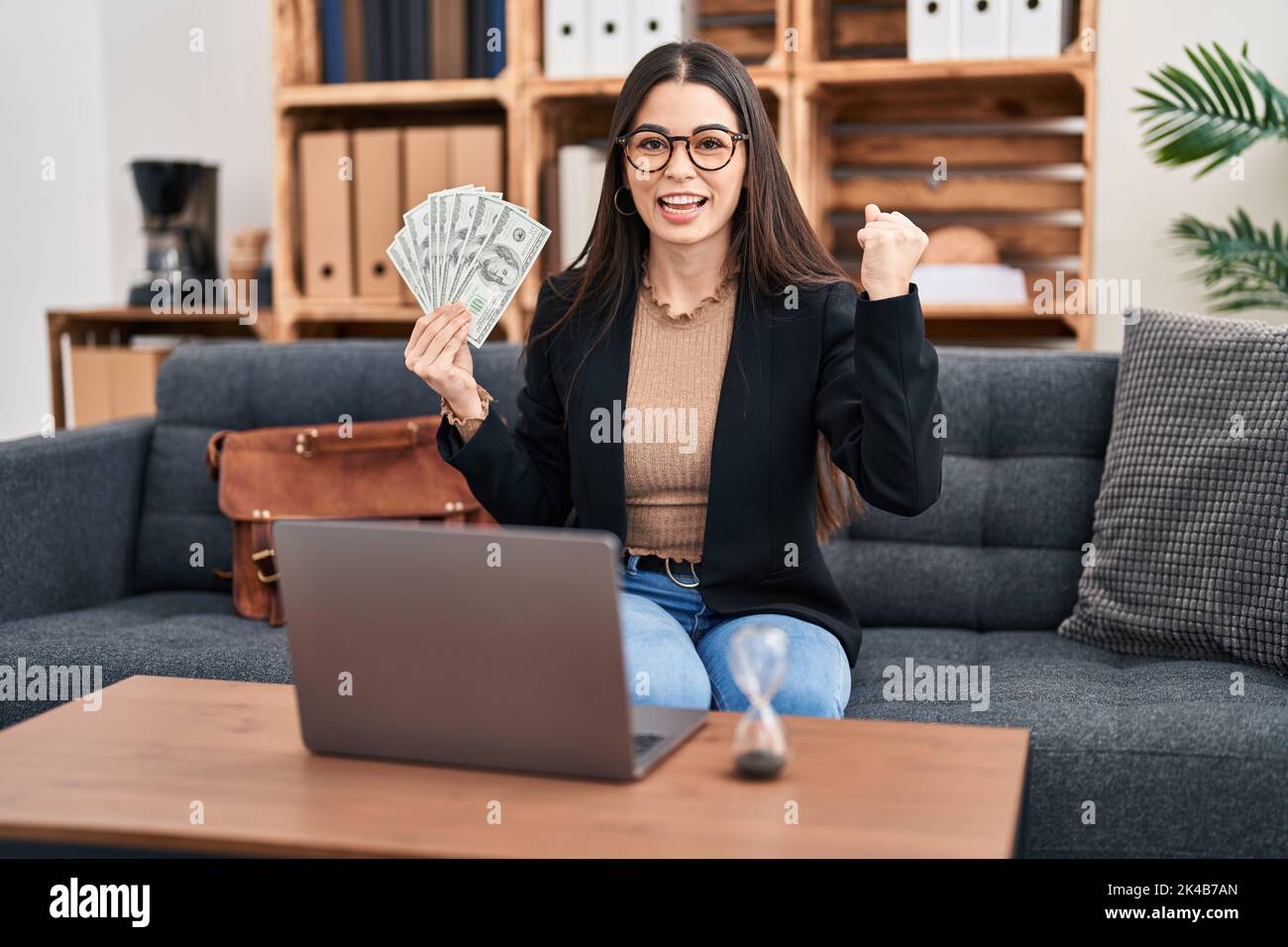 Young woman working at consultation office holding money screaming ...