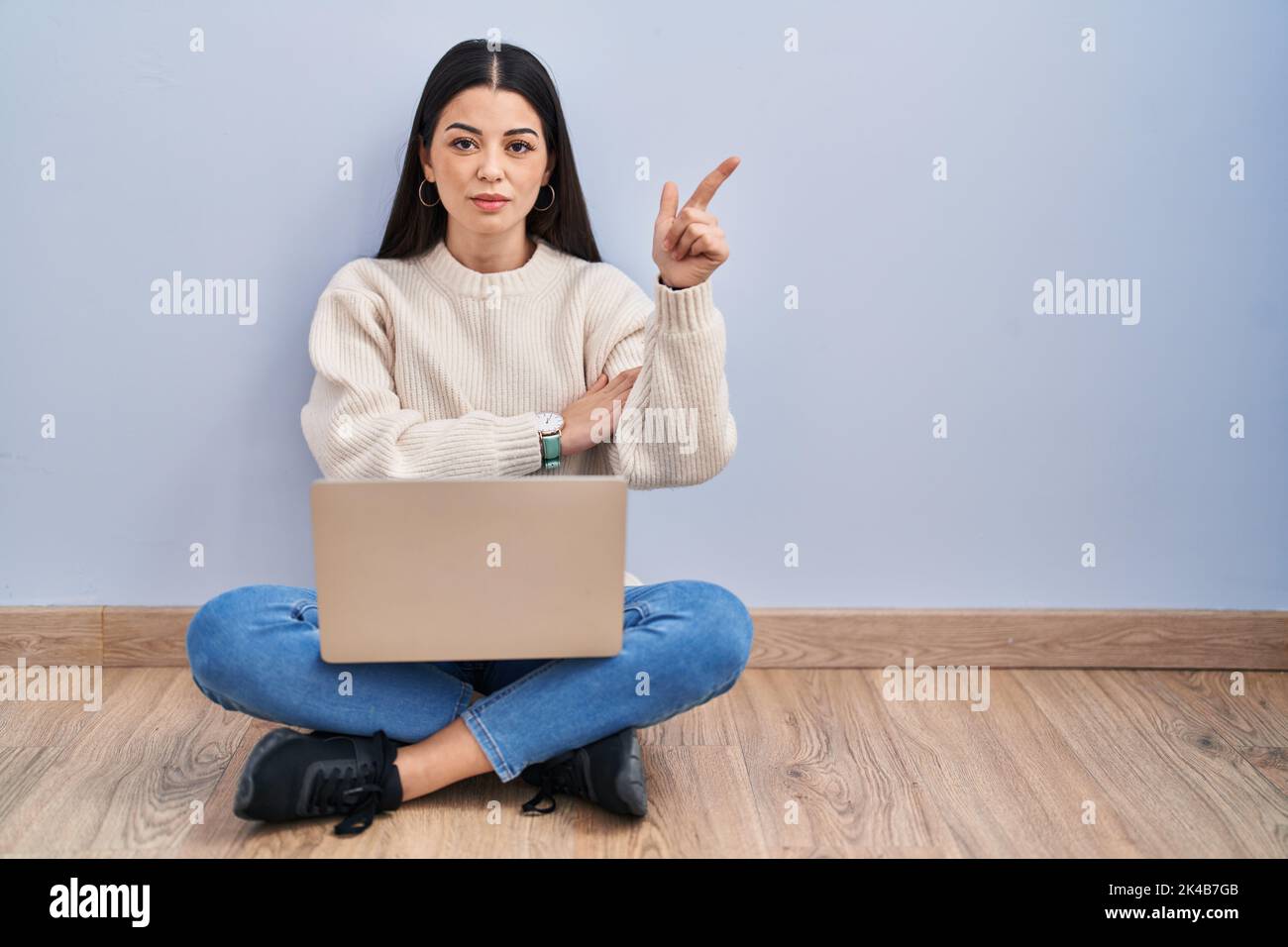 Young woman using laptop sitting on the floor at home pointing with ...