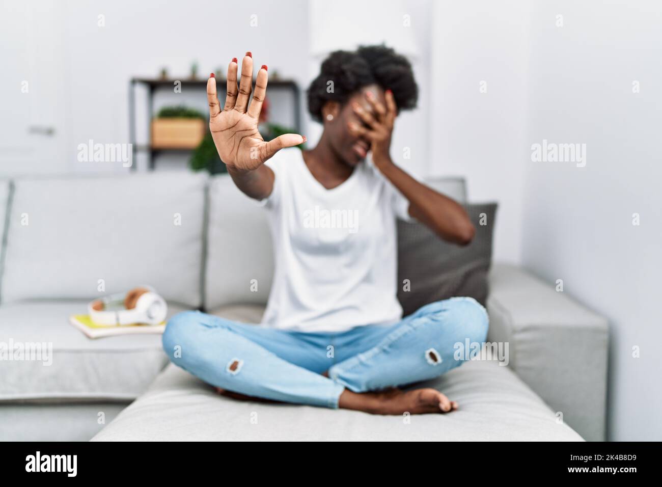 African young woman sitting on the sofa at home covering eyes with ...