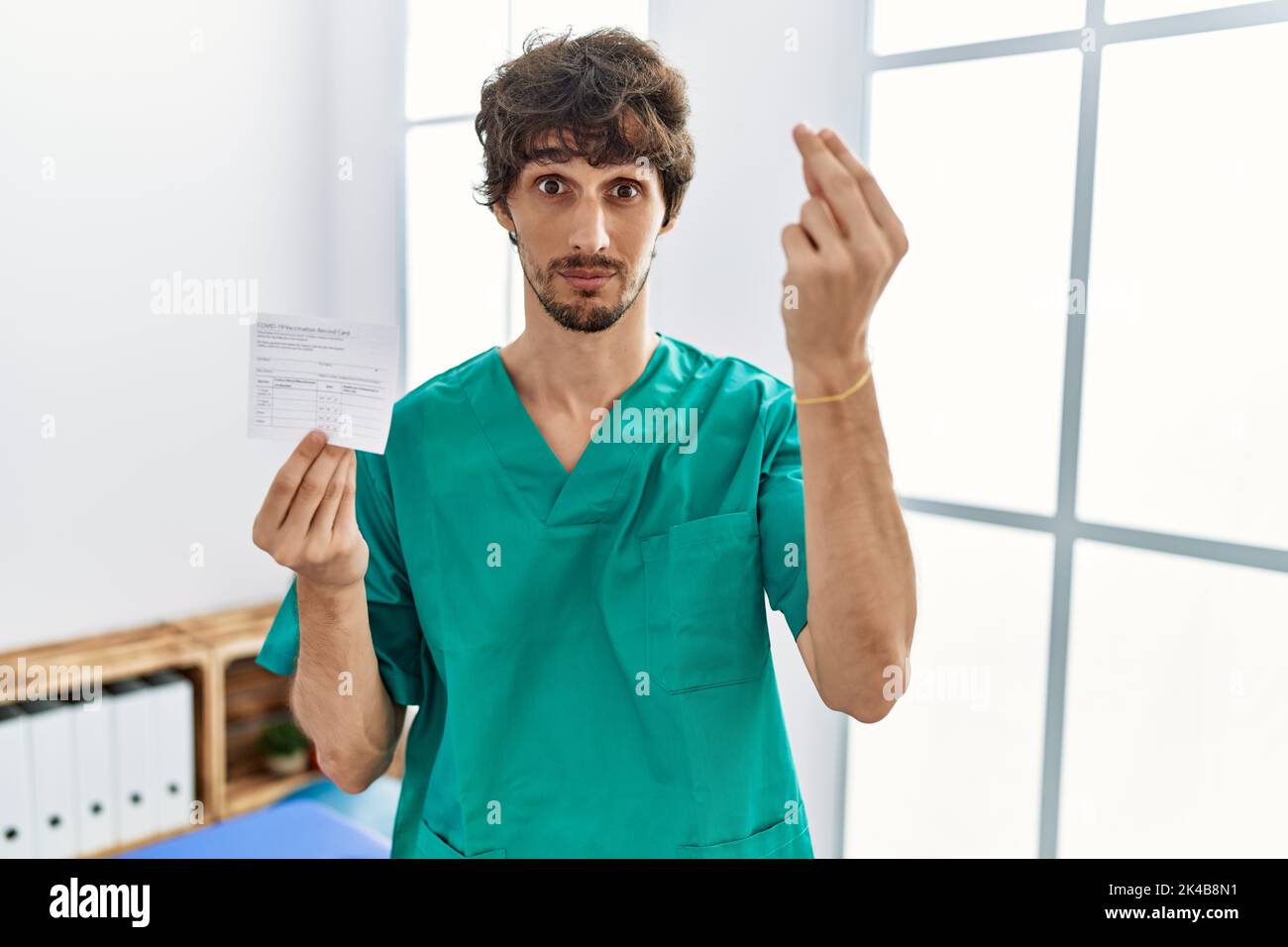Young hispanic doctor man holding covid record card doing italian ...