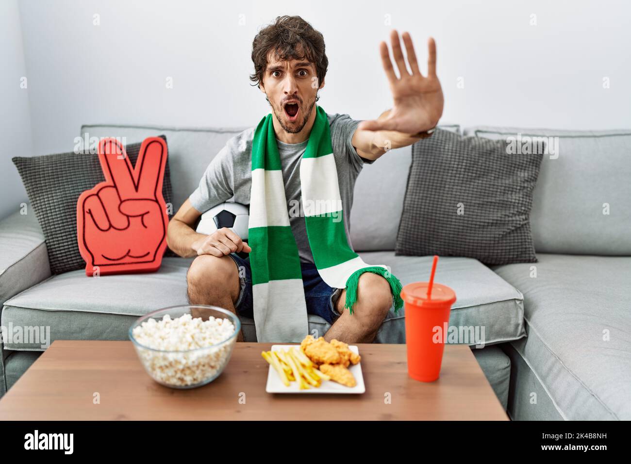 Young hispanic man football hooligan cheering game at home doing stop ...