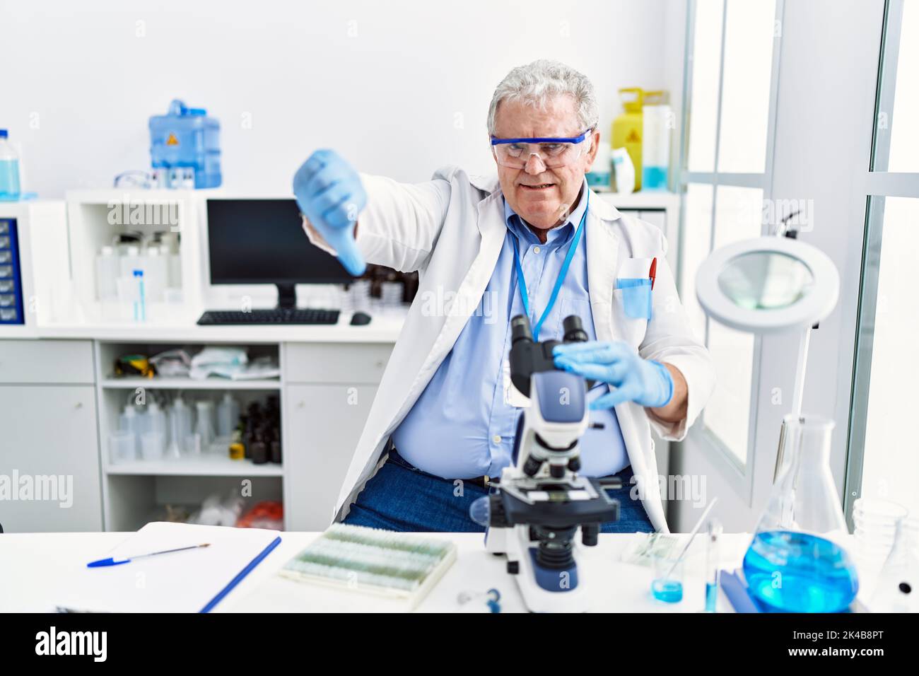 Senior caucasian man working at scientist laboratory looking unhappy ...