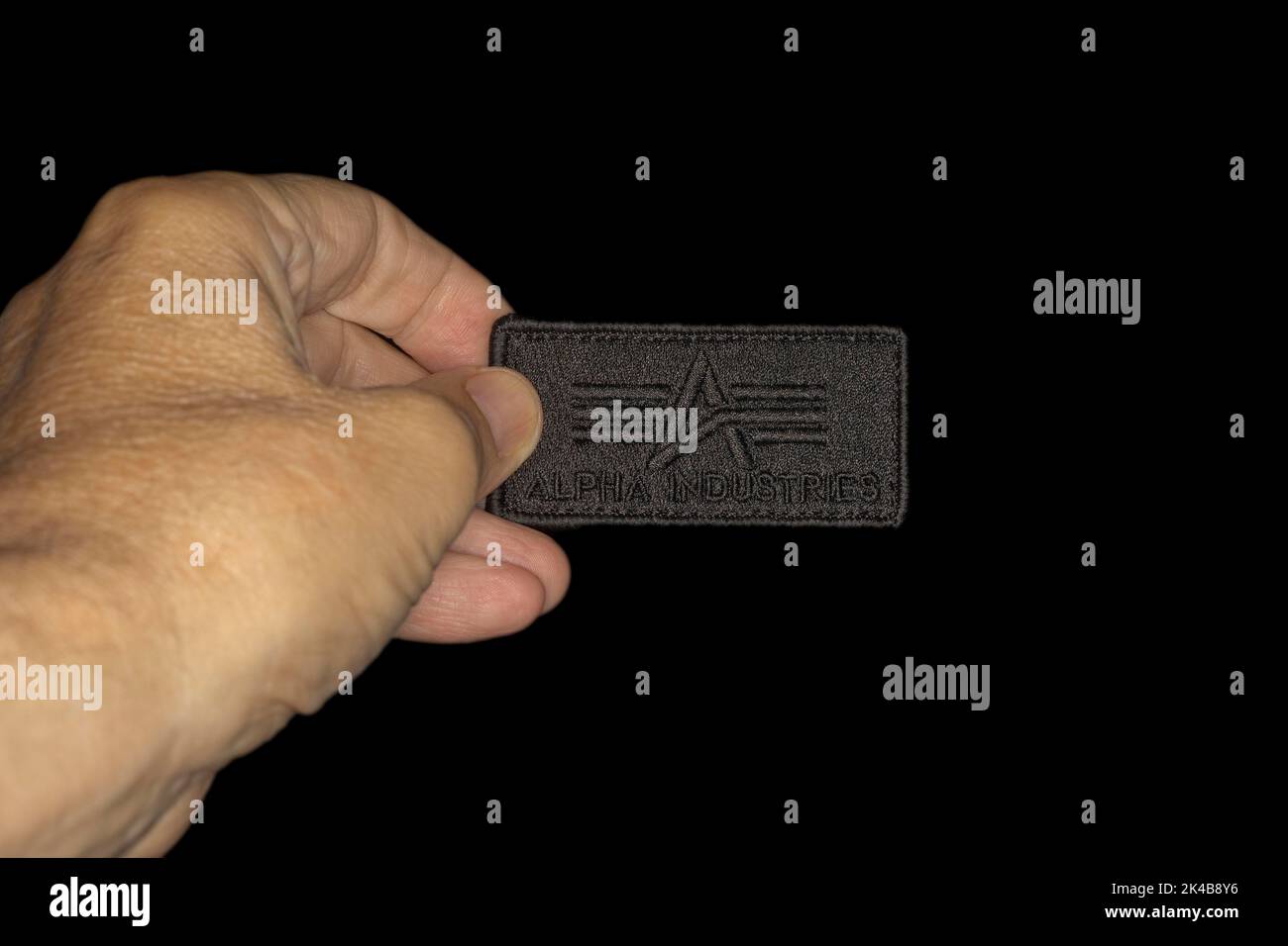 A man's hand holding a black patch of the company Alpha Industries ...
