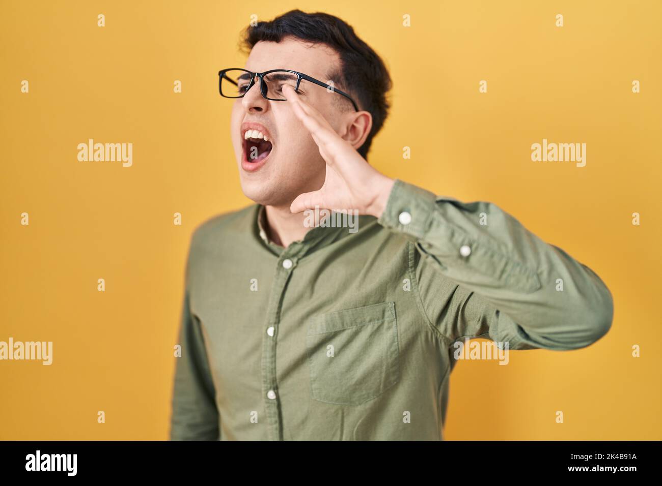 Non binary person standing over yellow background shouting and ...