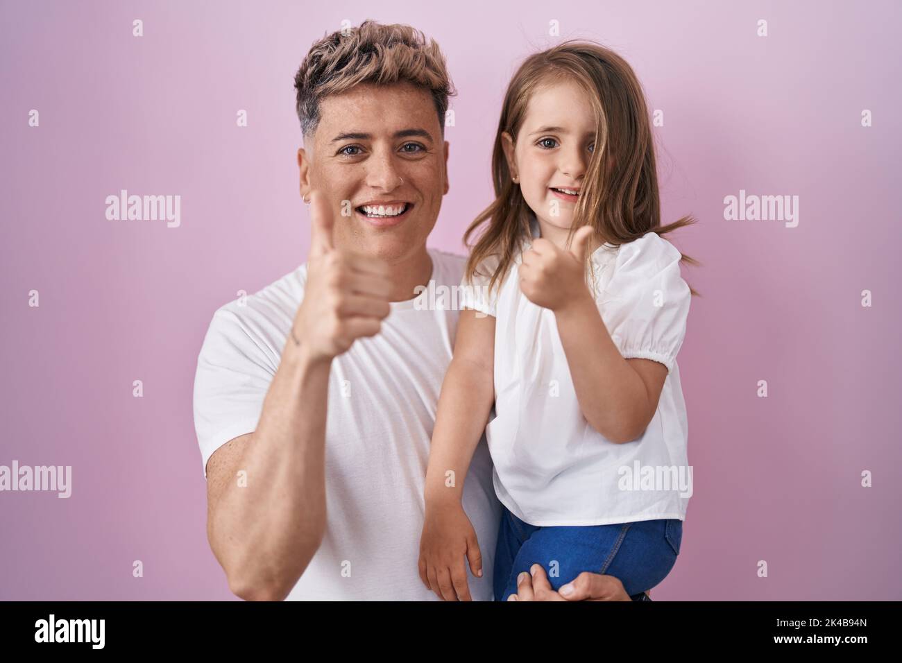 Young father hugging daughter over pink background smiling happy and ...