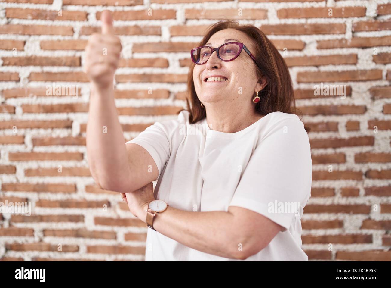 Senior woman with glasses standing over bricks wall looking proud ...