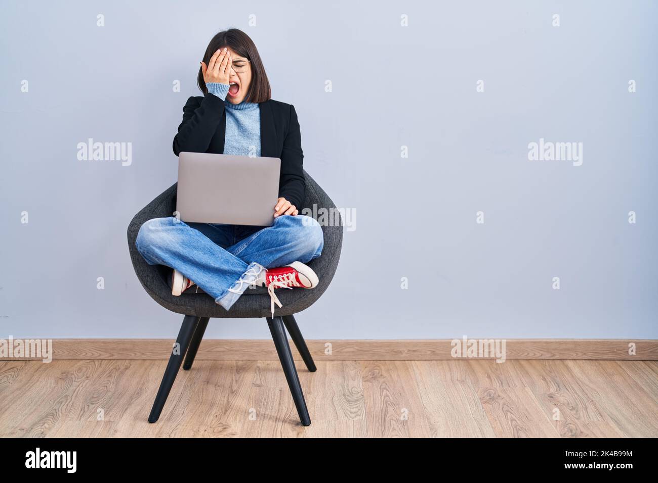 Young hispanic woman sitting on chair using computer laptop yawning ...