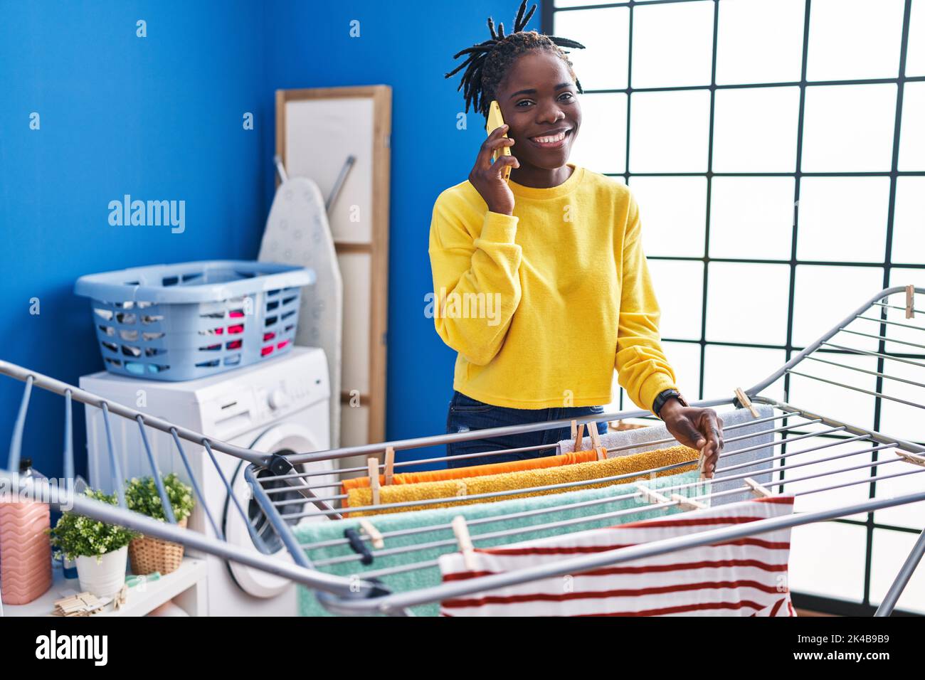African american woman talking on the smartphone hanging clothes on ...