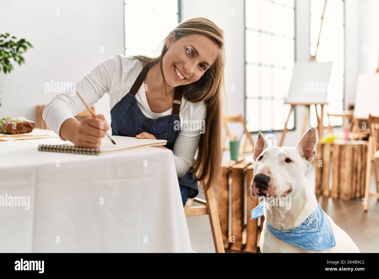 Young caucasian woman smiling confident drawing with dog at art studio ...