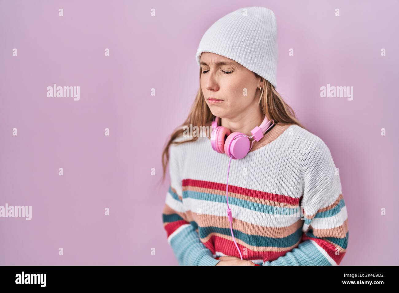 Young blonde woman standing over pink background with hand on stomach ...
