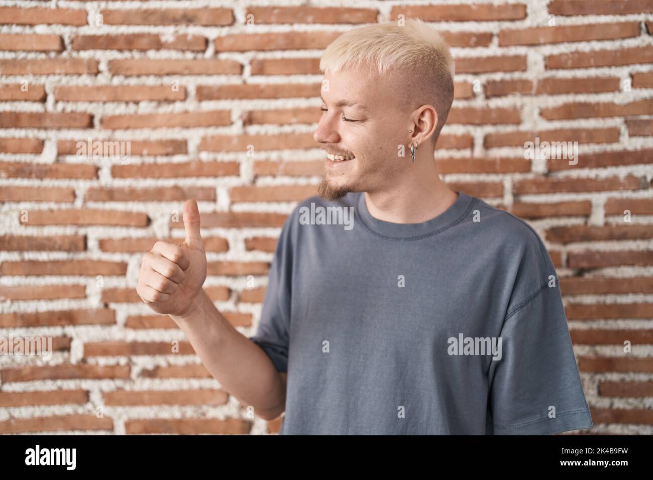 Young caucasian man standing over bricks wall looking proud, smiling ...