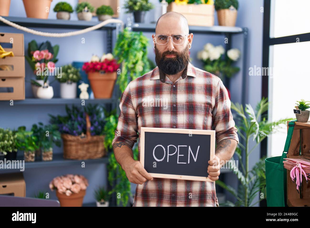 Young hispanic man with beard and tattoos working at florist holding ...