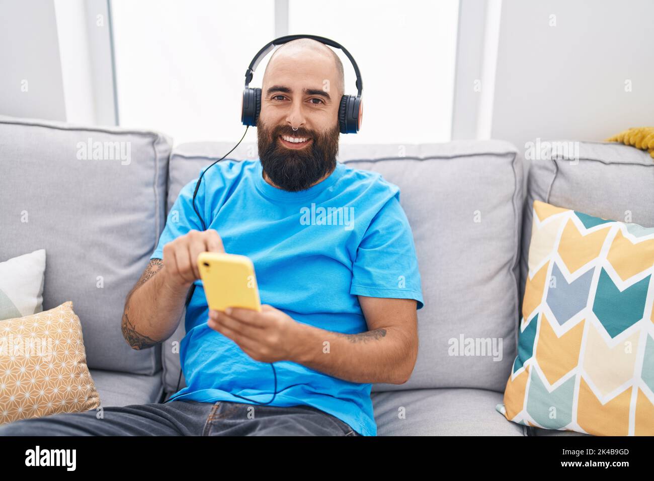 Young bald man listening to music sitting on sofa at home Stock Photo ...