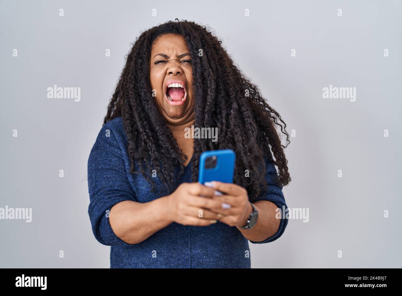 Plus size hispanic woman using smartphone typing message angry and mad ...