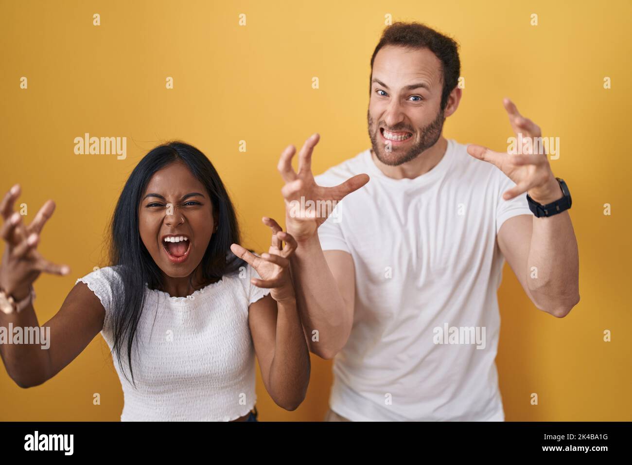 Interracial couple standing over yellow background shouting frustrated ...
