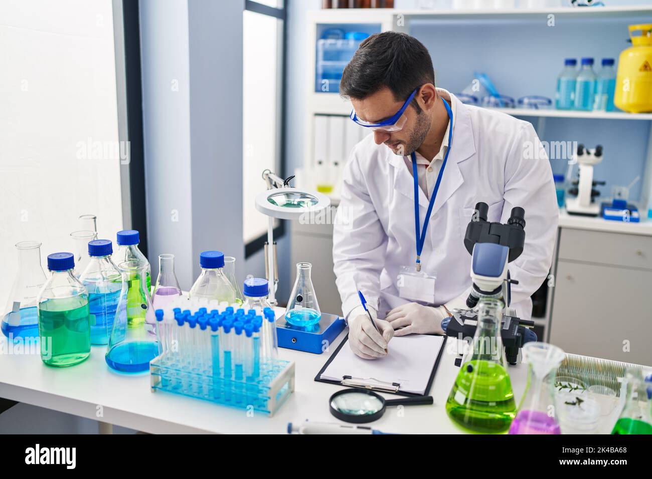 Young hispanic man scientist measuring liquid writing report at ...