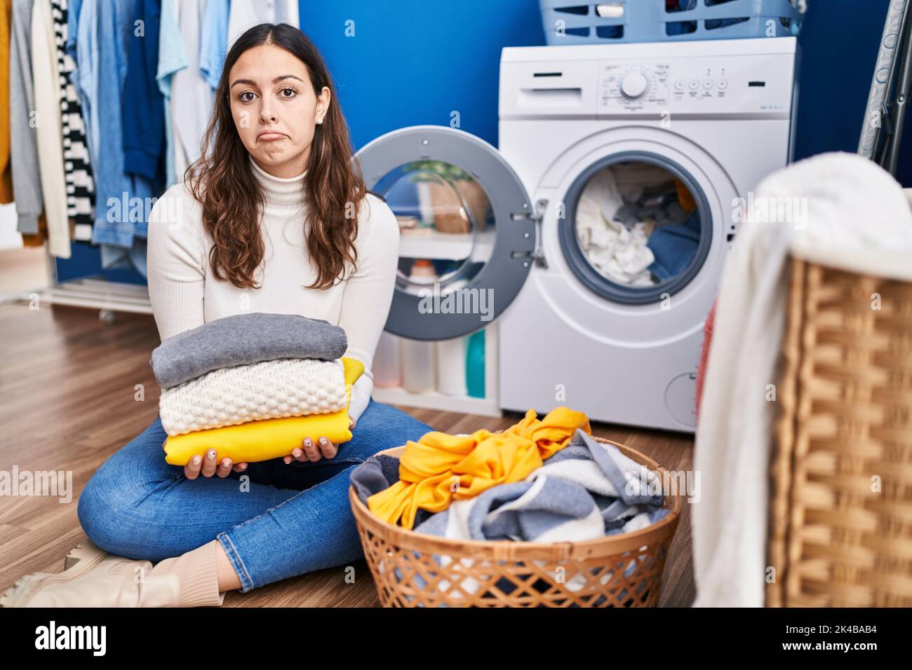 Young hispanic woman holding clean laundry depressed and worry for distress, crying angry and ...