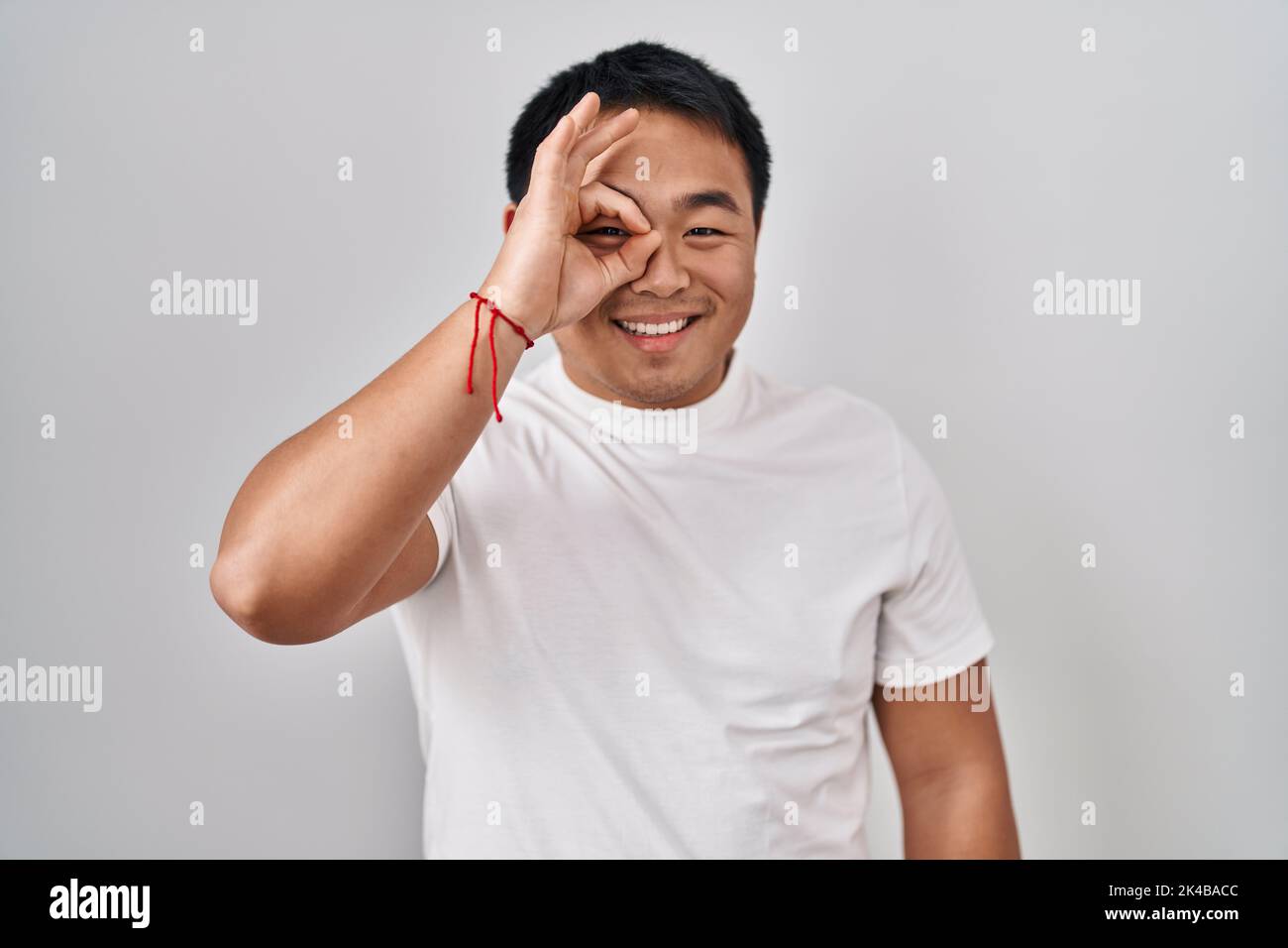 Young chinese man standing over white background doing ok gesture with ...