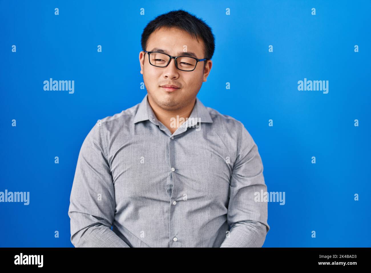 Young chinese man standing over blue background smiling looking to the ...