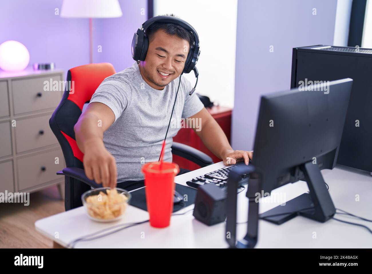 Young chinese man streamer playing video game eating chips potatoes at ...
