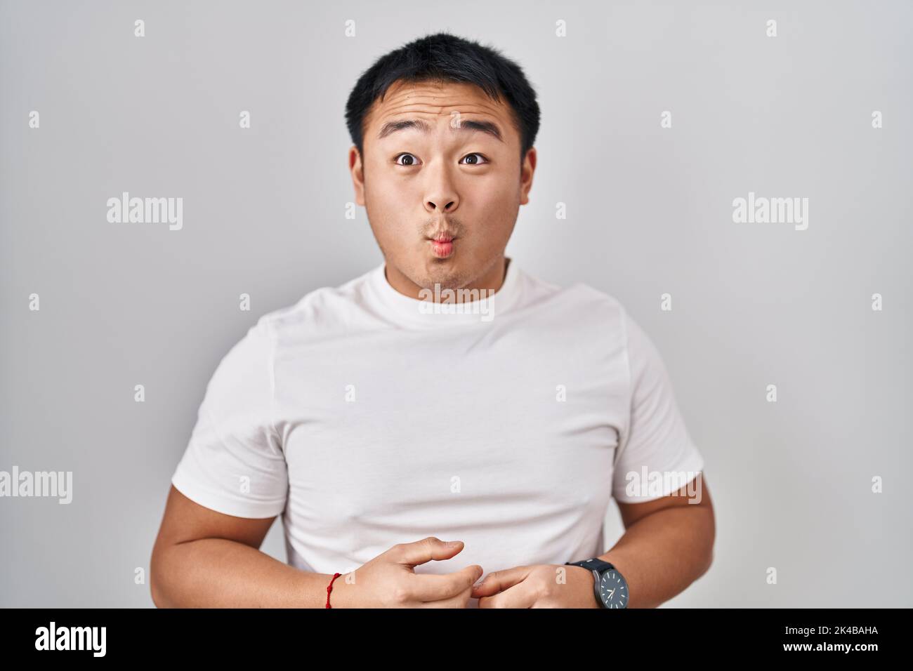 Young chinese man standing over white background making fish face with ...