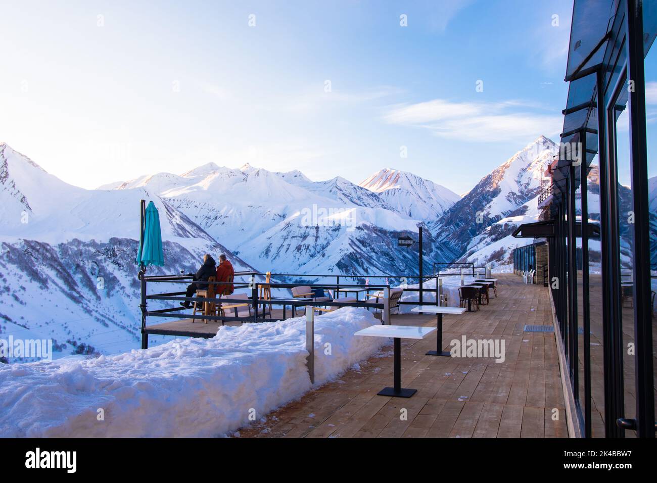 Couple together sit enjoy sunset in winter ski resort with snowy peaks ...