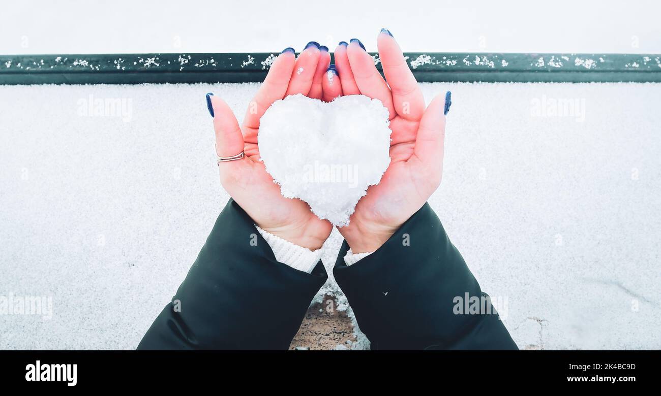 Top down view woman in two hands hold ice heart made of snow. Girl give ...