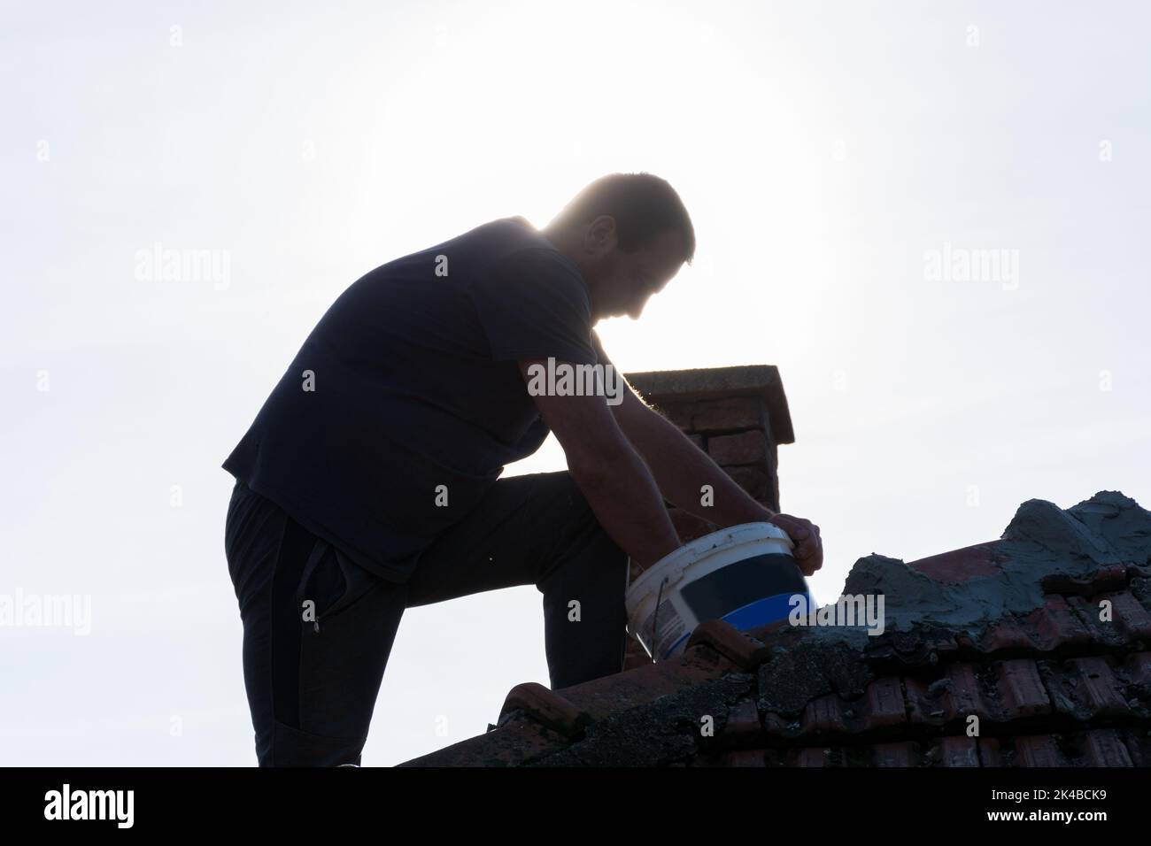 Worker secure and patch roof tiles with cement on an old building roof ...