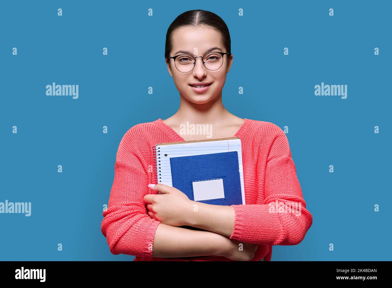 Portrait of teenage female student holding notebooks looking at camera ...