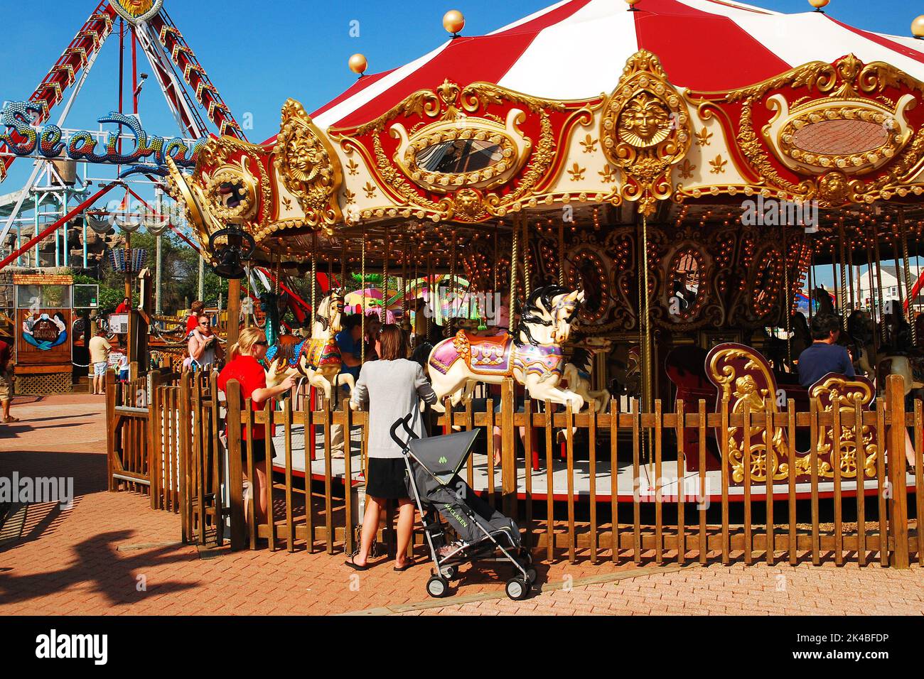 A mother watches as her children ride a carousel merry go round at a ...