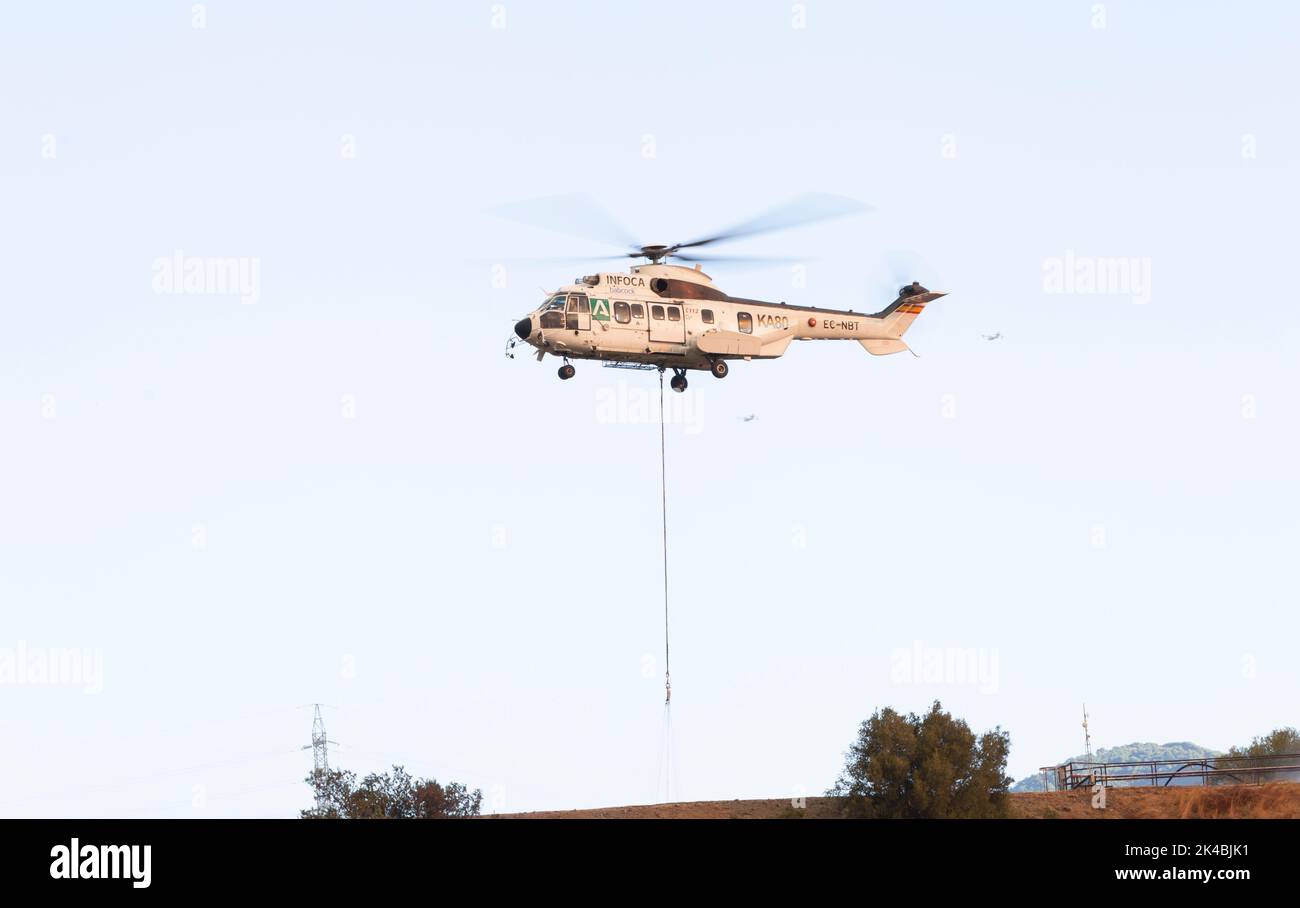 A White Airbus Helicopters H215 refilling a water bucket as it works ...