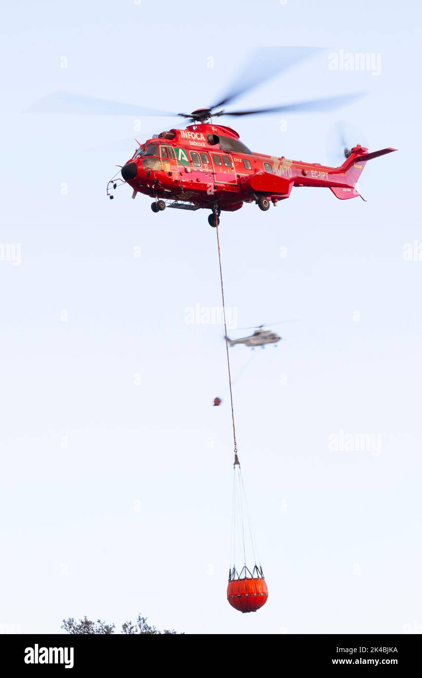 A Red Airbus Helicopters H215 refilling a water bucket as it works ...
