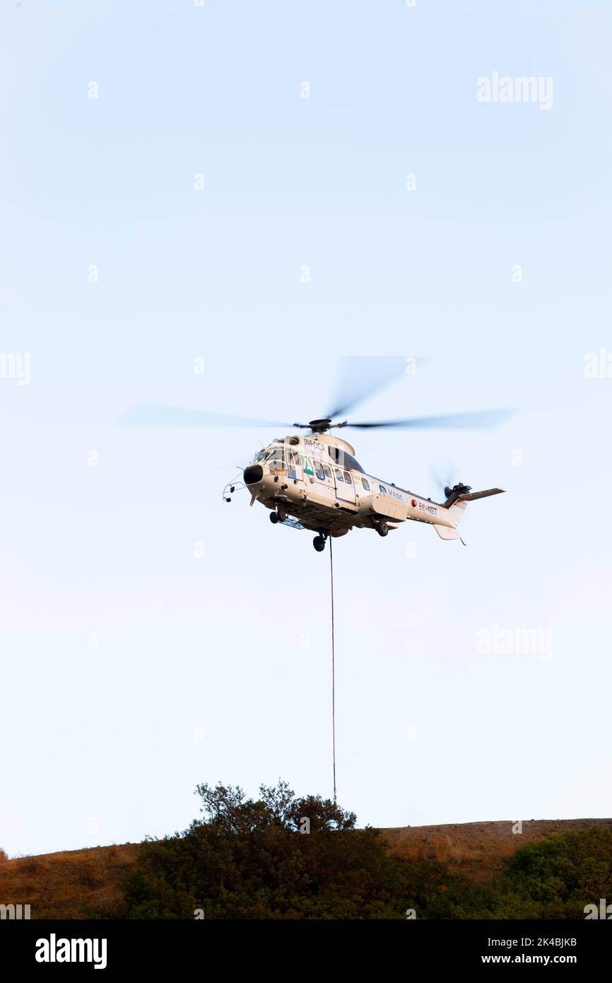 A White Airbus Helicopters H215 refilling a water bucket as it works ...