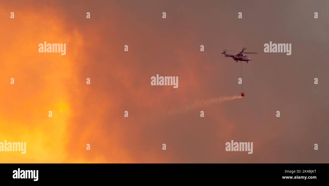 A Red Airbus Helicopters H215 rushes with its water bucket towards the ...