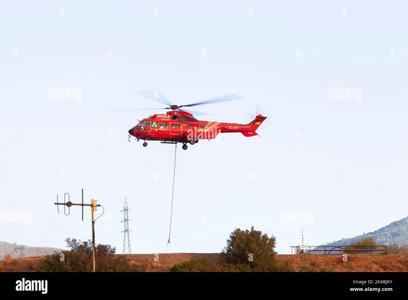 A Red Airbus Helicopters H215 refilling a water bucket as it works ...