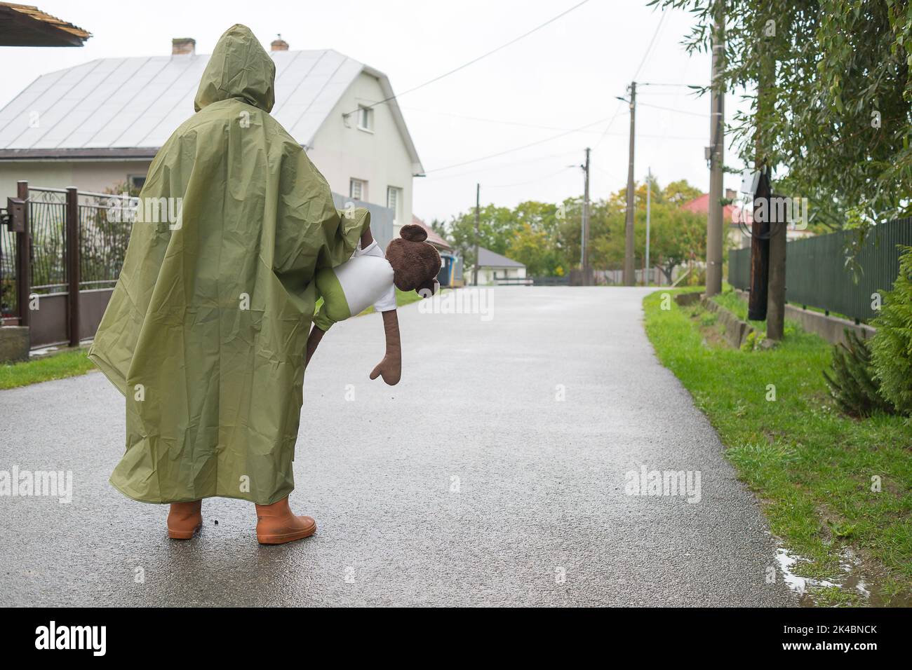 Boy wearing green raincoat standing on road during rainy day. Child ...
