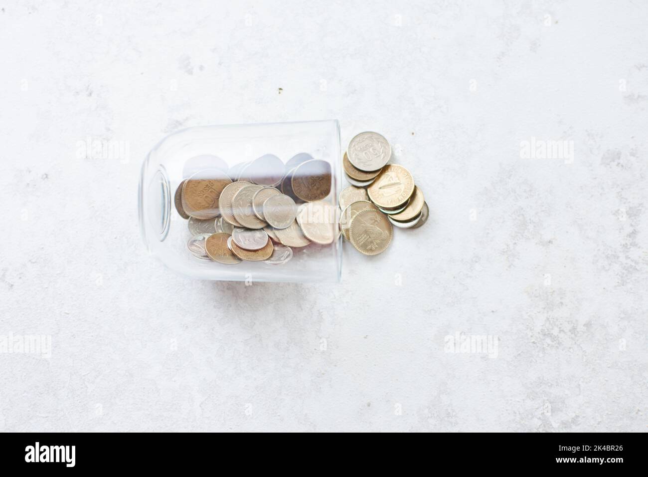A glass cup falling on a white surface with Colombia Peso banknotes and ...