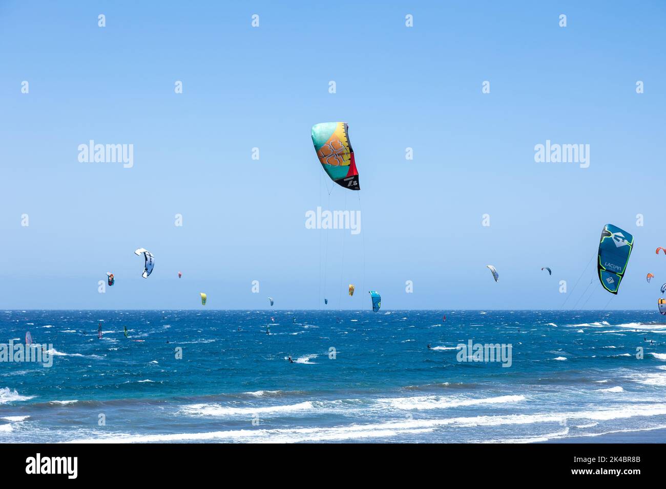 A shot of the ocean on a sunny day while people kitesurf on the water ...