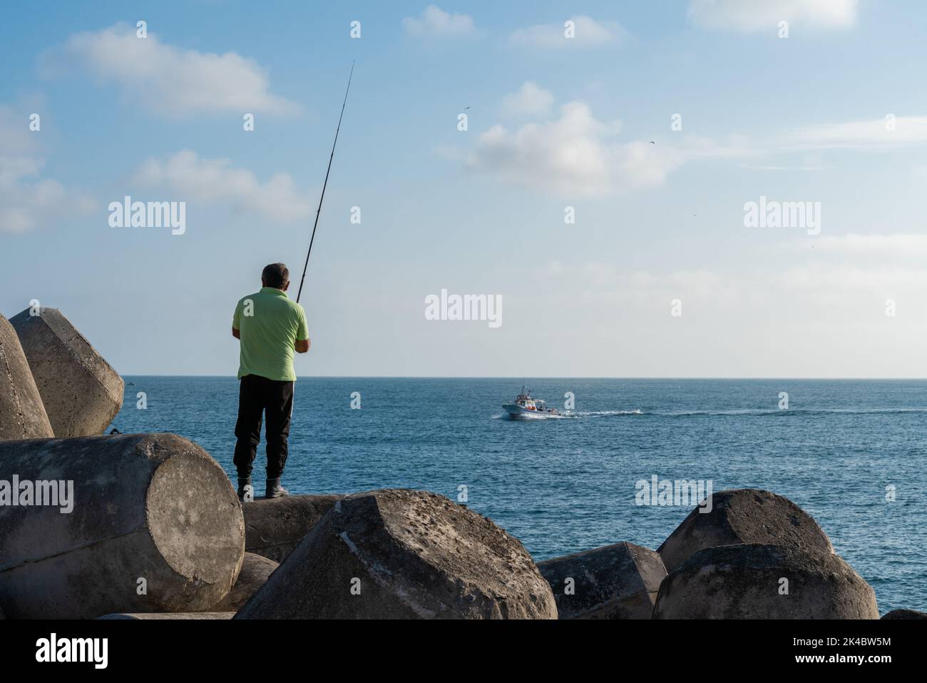 A back view of a fisherman on a shore and the fishing boat on the ...