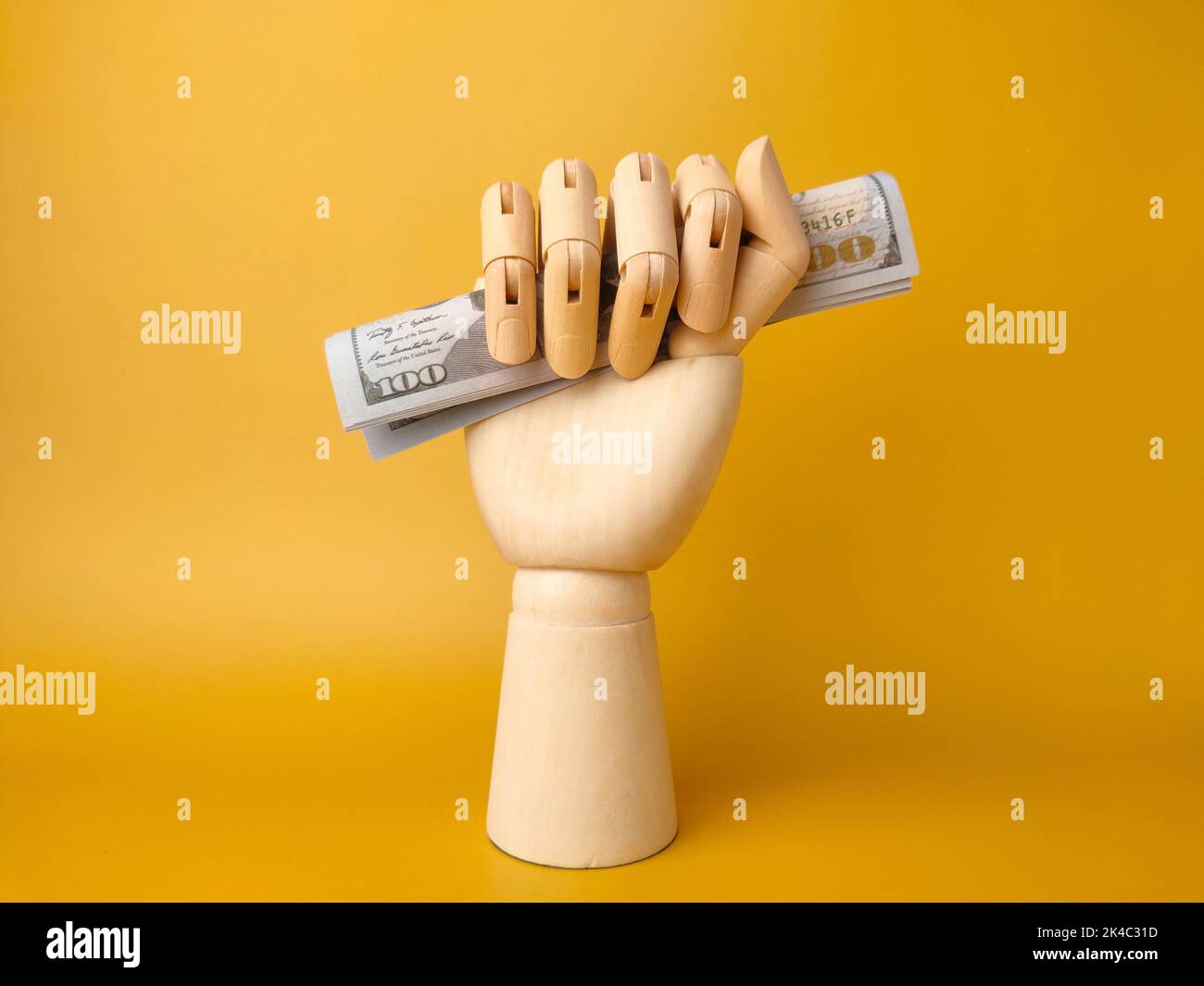 A wooden hand gripping banknotes on a yellow background Stock Photo - Alamy
