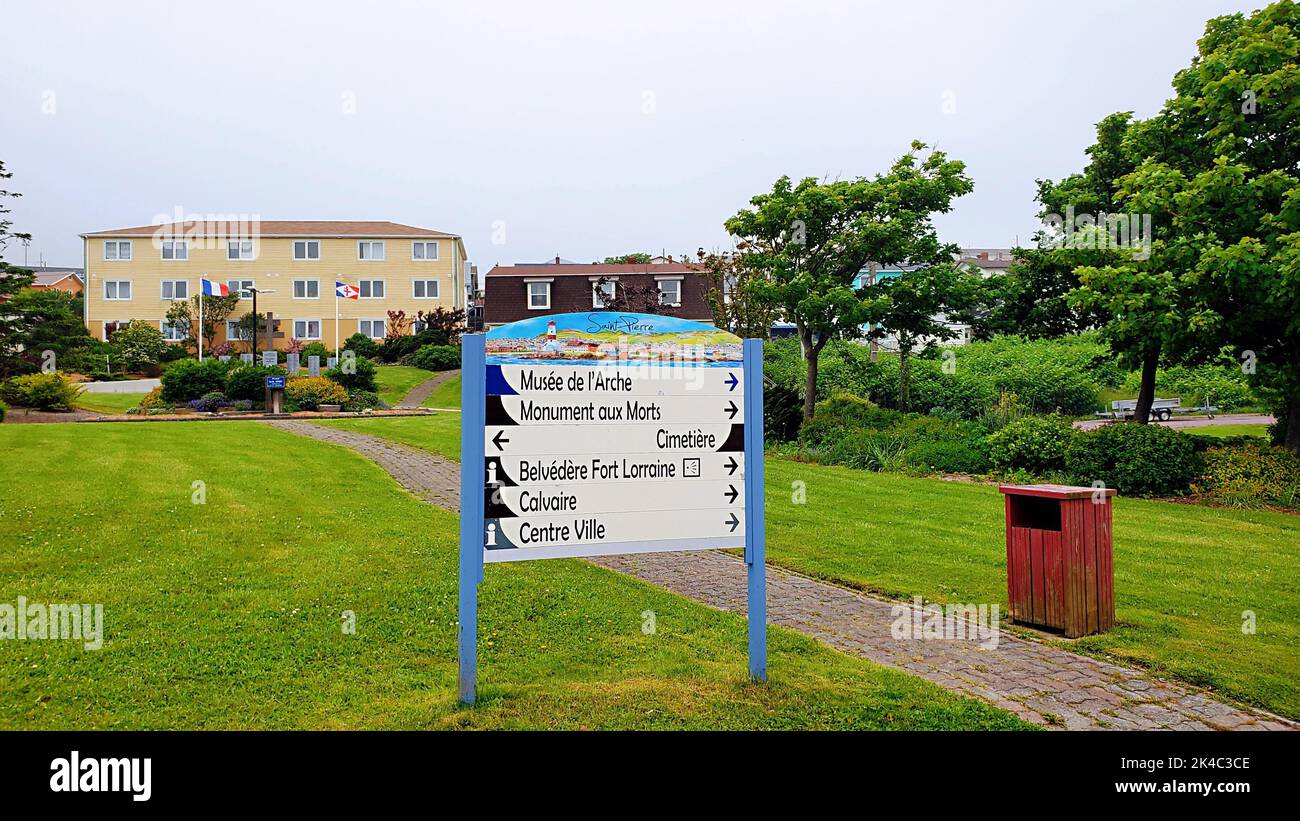An outdoor sign in a beautiful garden with buildings in background ...