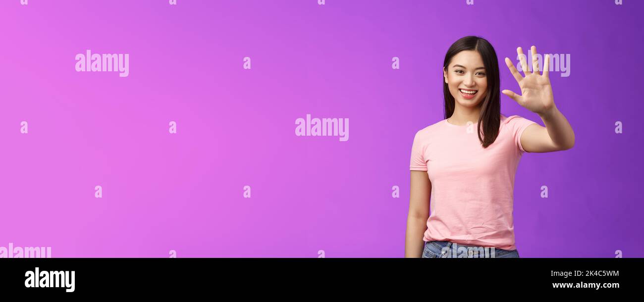 Friendly cute asian tender girl raise palm waving goodbye, smiling ...