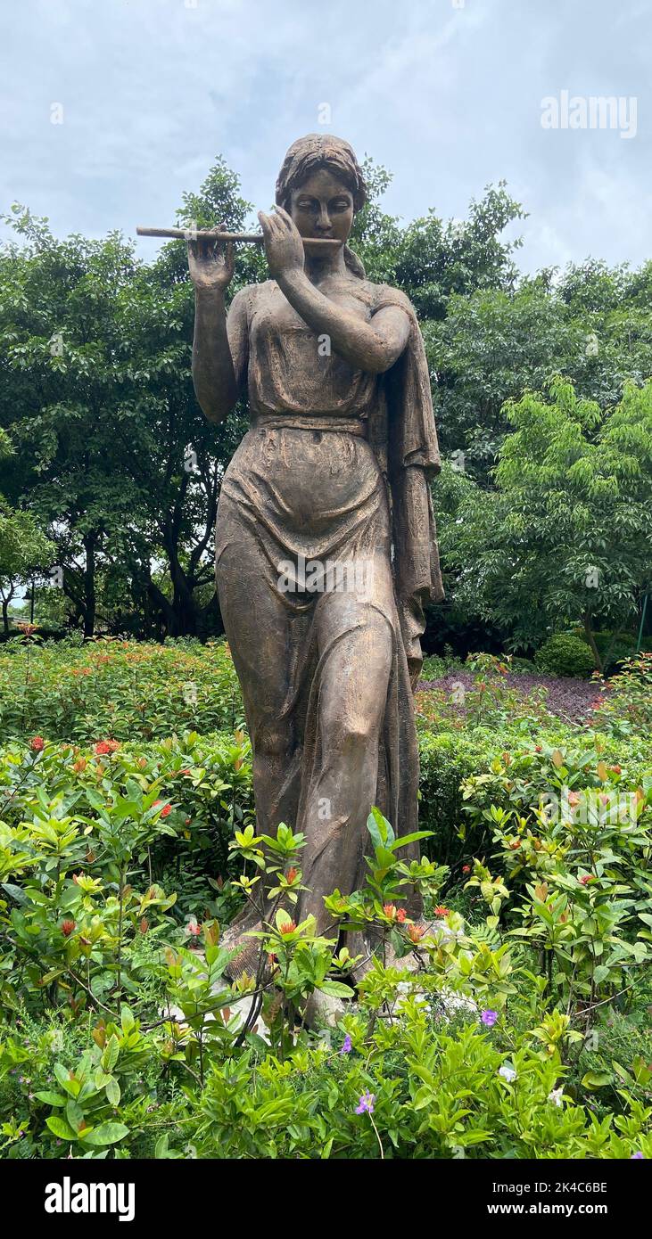 A vertical shot of a bronze statue of woman playing flute at the park ...