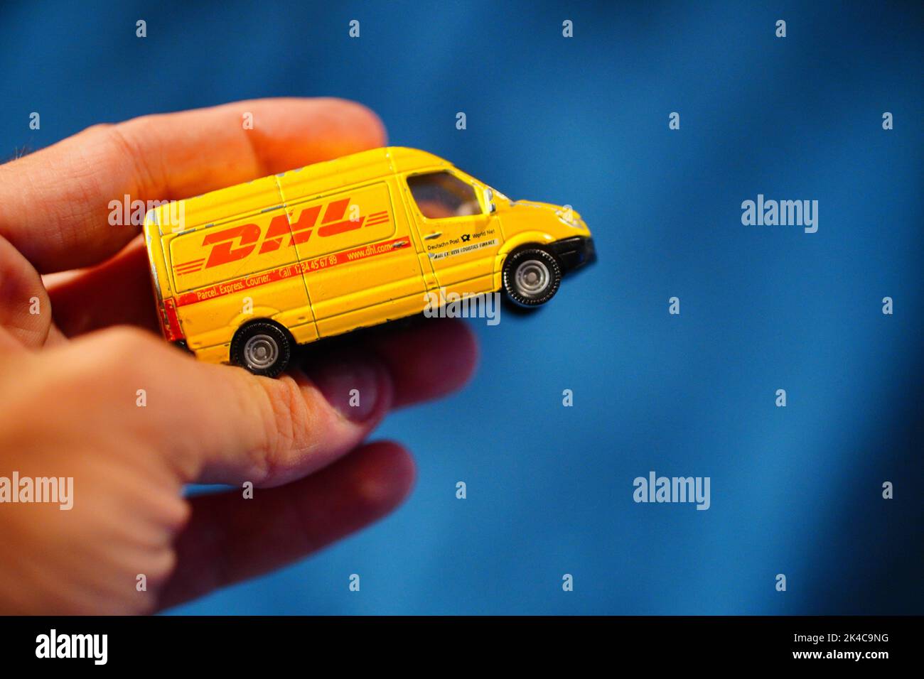 A closeup shot of a hand holding a Siku brand yellow DHL toy model van ...