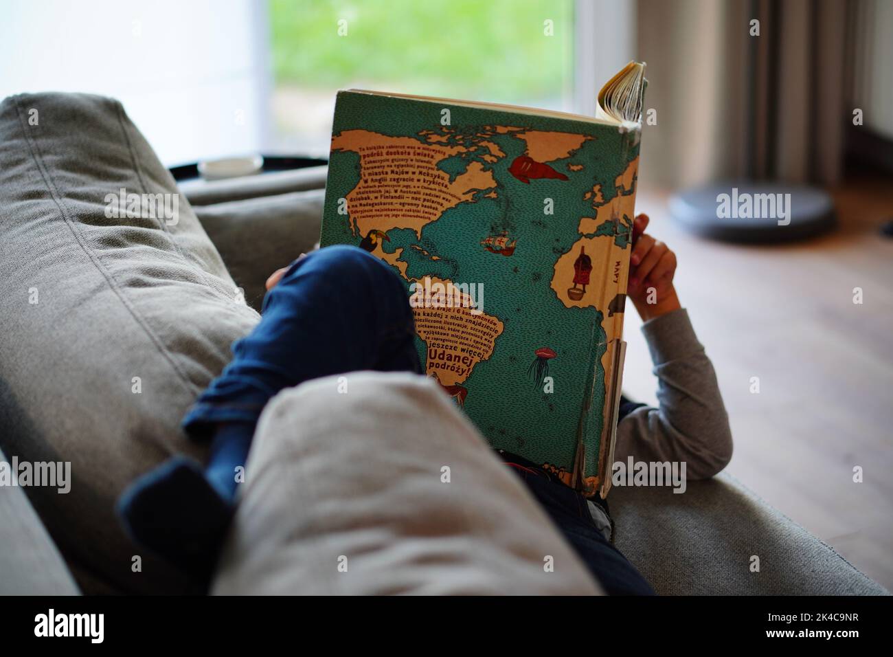 A young boy lying on a couch and reading a Polish atlas for children ...
