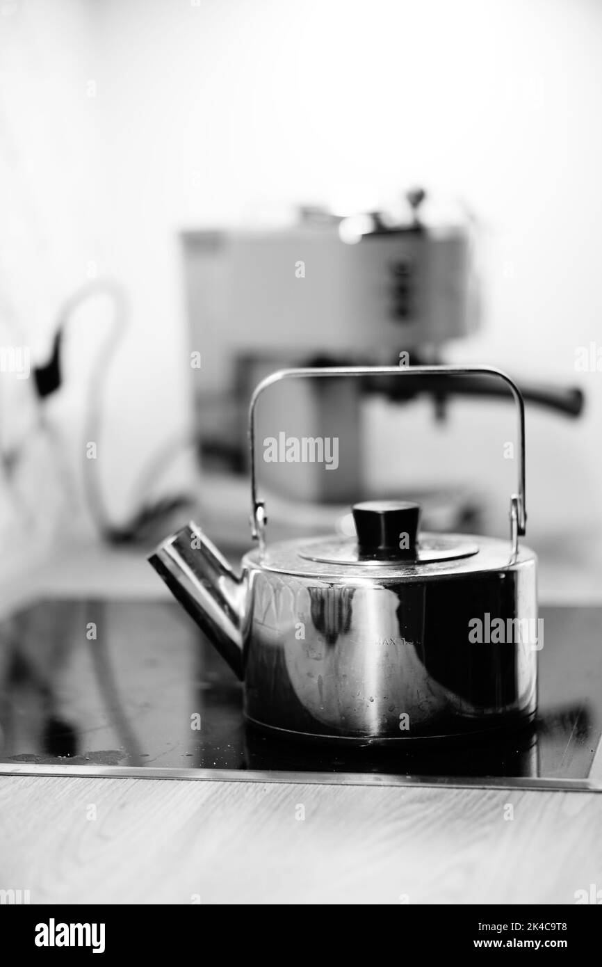 A grayscale vertical shot of a metal kettle on an Amica cooker in a ...
