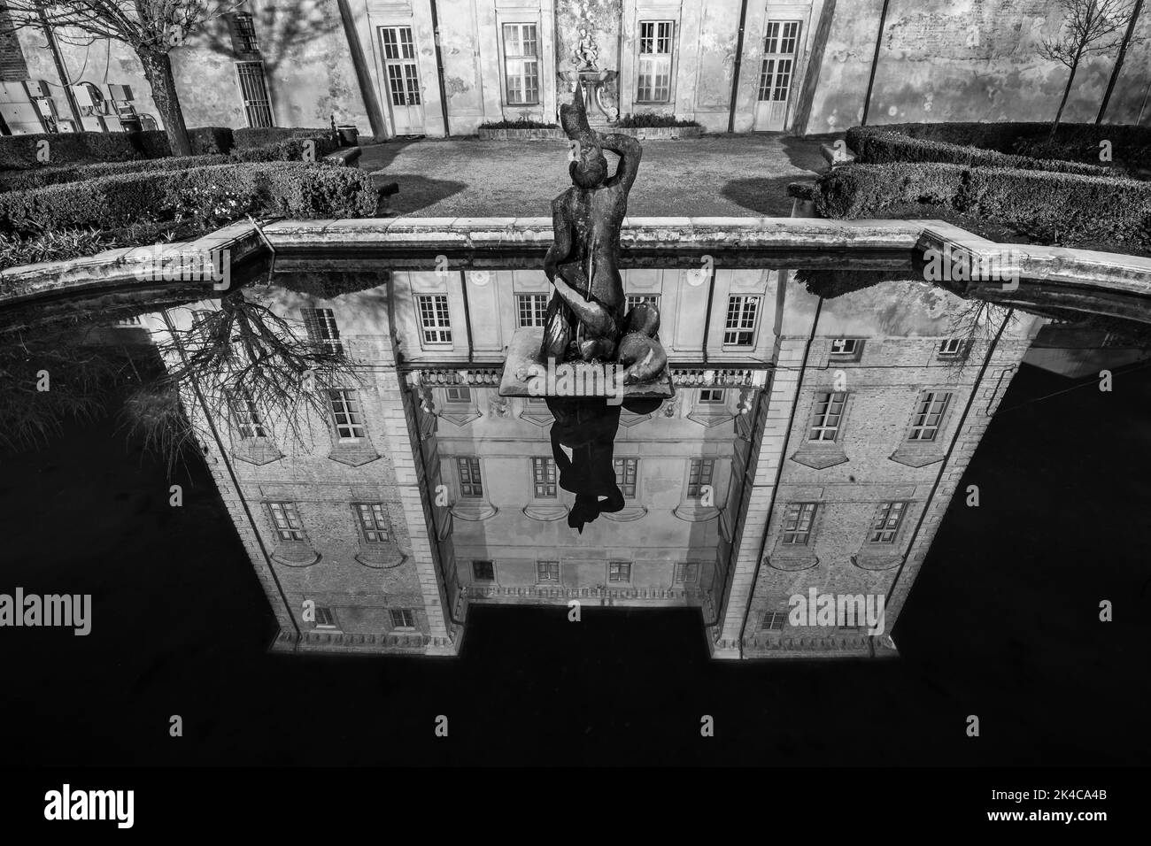 A grayscale shot of statue in fountain with the reflection of building ...