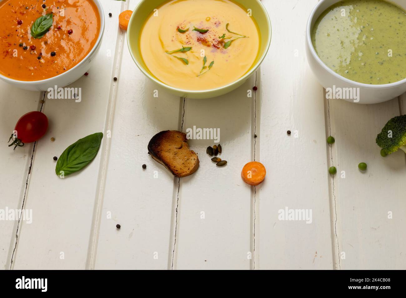 Horizontal image of bowls of carrot, broccoli and tomato soups on white ...