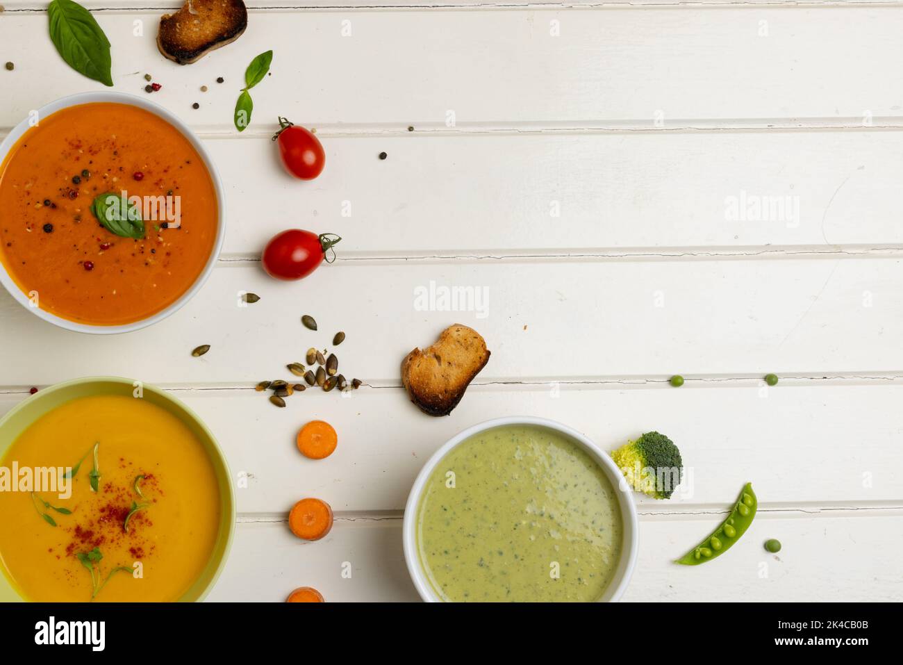 Horizontal image of bowls of carrot, broccoli and tomato soups on white ...