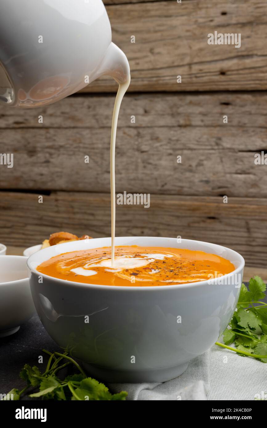 Vertical image of cream pouring into bowl of tomato soup, with wood ...